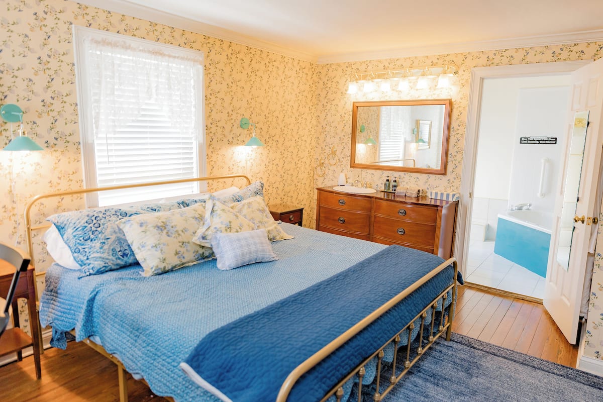 Quarto com cama, cómoda, espelho e porta para uma casa de banho.