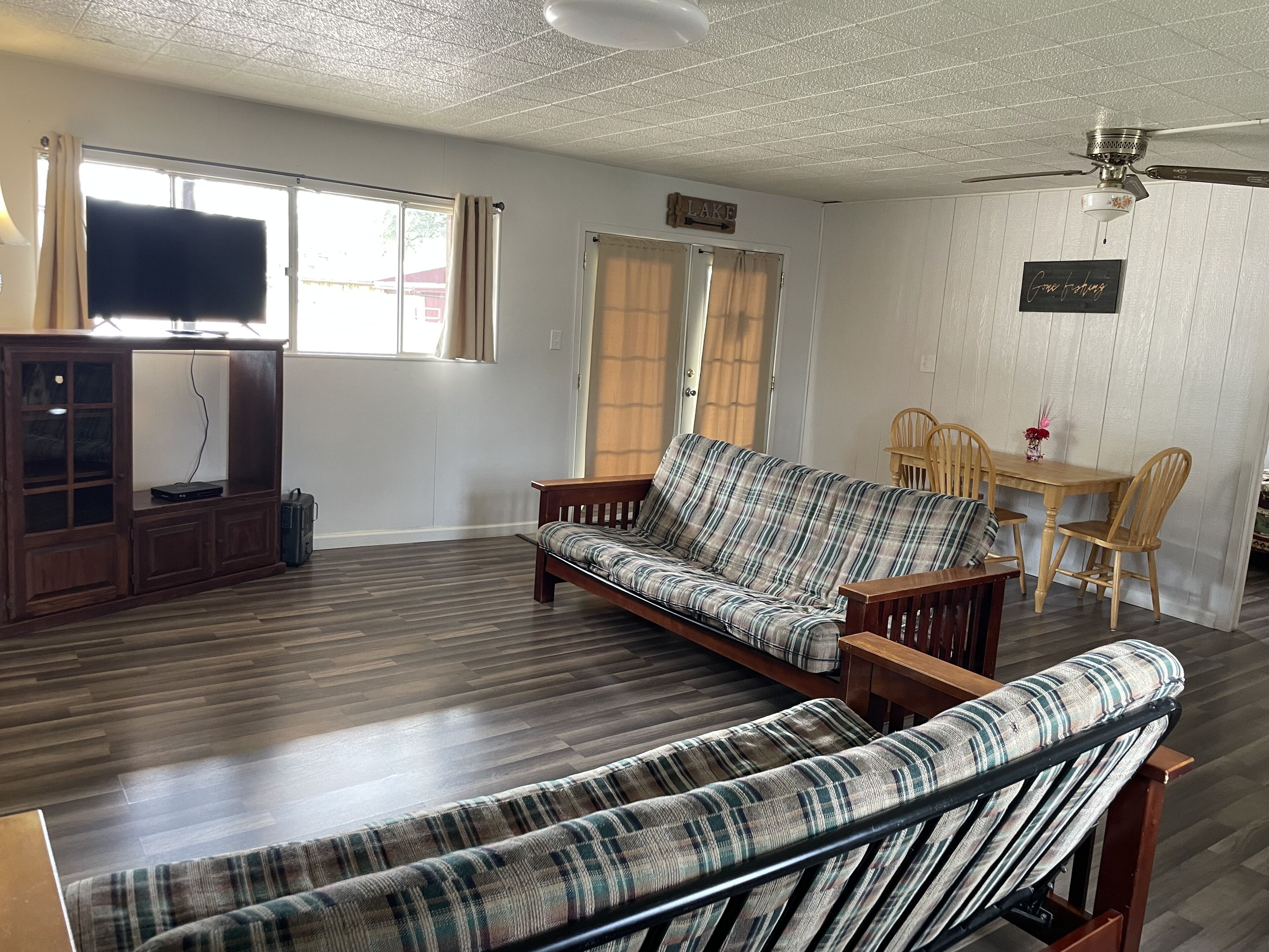 Sala de estar com sofá, mesa de jantar de madeira, cadeiras, televisão em um móvel e ventilador de teto.