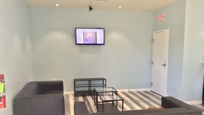Quarto com televisão de tela plana na parede, um sofá, uma mesinha e uma porta.