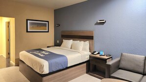Quarto de hotel com cama, mesa de cabeceira, cadeira e uma pequena mesa.