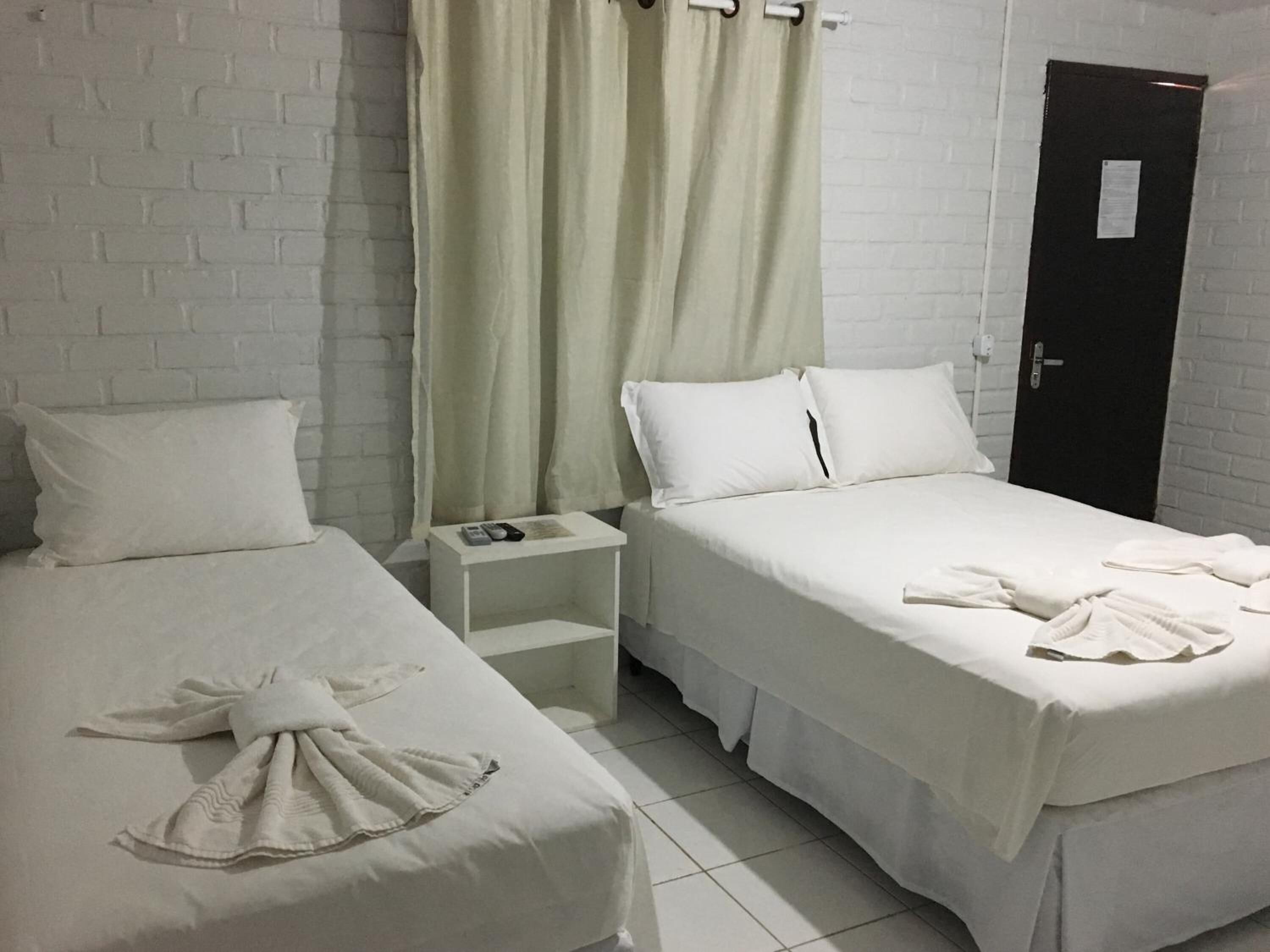 Quarto de hotel com duas camas, uma mesa de cabeceira e uma porta.