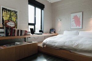 Um quarto com uma cama, uma escrivaninha com livros, um computador e uma janela.