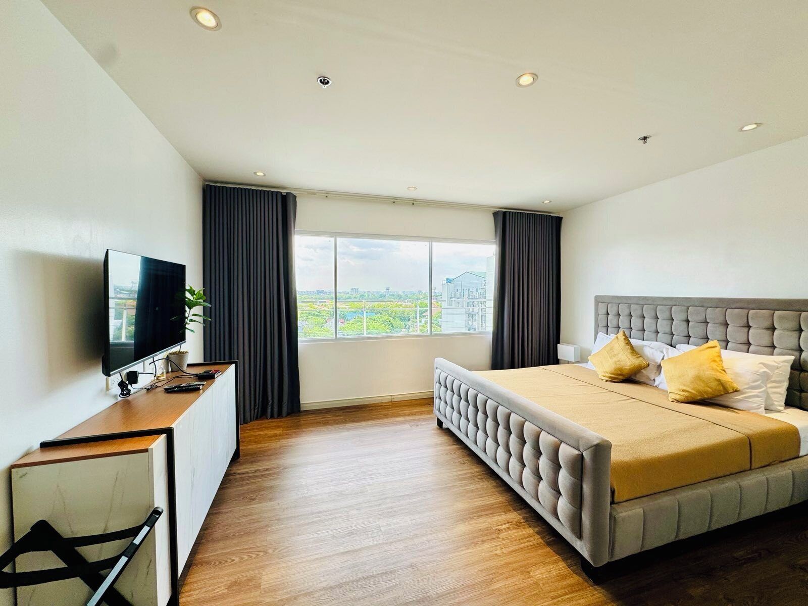 Quarto de hotel moderno com uma cama grande, uma escrivaninha com televisão e vista para a cidade.