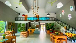 Um hall amplo com teto alto, mobiliário de madeira, uma escadaria e um balcão de recepção.