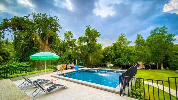 Piscina com deck ladrilhado, guarda-sol verde e cadeiras de descanso.