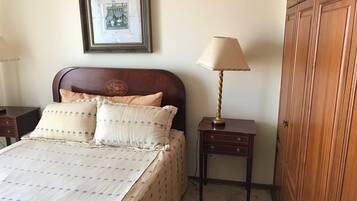 Quarto bem arrumado com cama, mesas de cabeceira, abajur, quadro emoldurado e guarda-roupa de madeira.