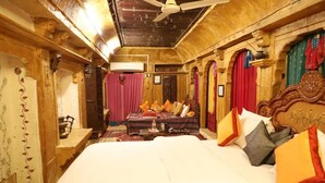 Quarto tradicional com uma cama grande, uma mesinha e um ventilador de teto.