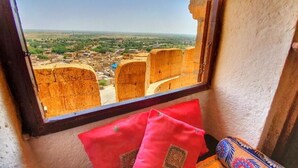 Quarto com janela que dá para uma fortaleza histórica e a paisagem urbana.
