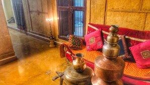 Quarto tradicional com piso de madeira, fogão de latão e recipiente de água em latão.