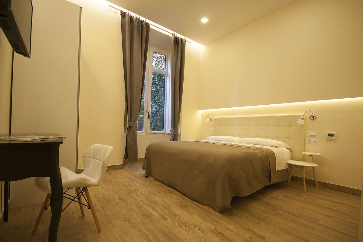 Um quarto com uma cama, uma cadeira, uma mesinha e uma janela com cortinas.