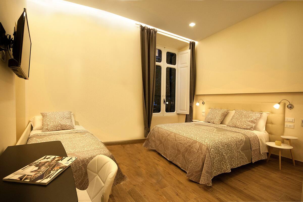Quarto de hotel com duas camas, uma mesa e janela com cortinas.