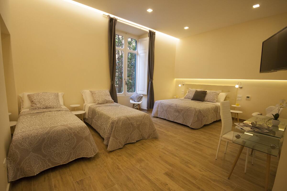Quarto de hotel com duas camas de solteiro, uma mesa de vidro e uma janela grande com cortinas.