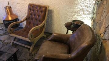 Um quarto rústico com uma poltrona de couro e uma cadeira estofada, uma pequena mesa com uma tigela de metal e uma panela de cobre.
