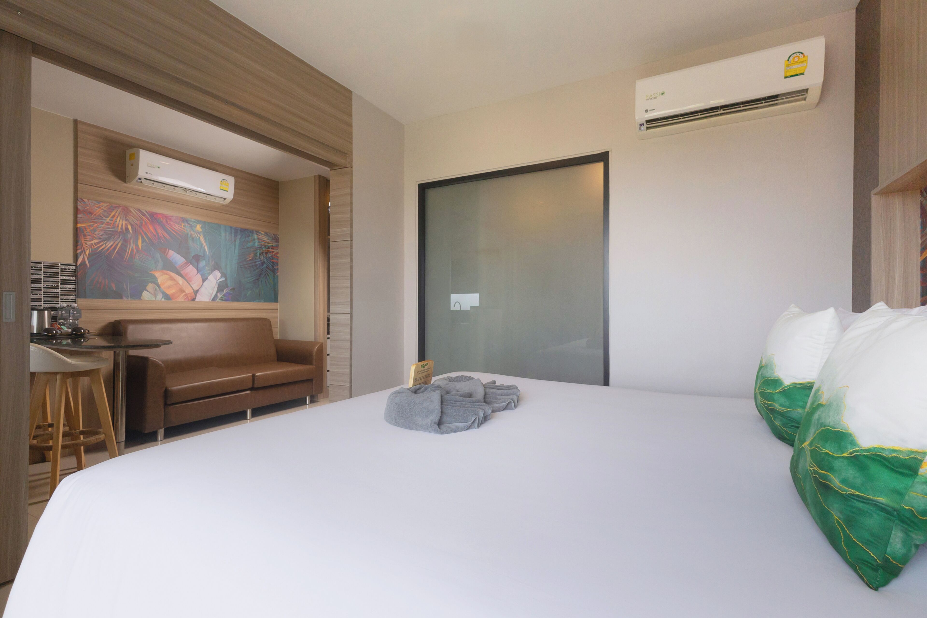 Quarto de hotel com cama, escrivaninha, sofá marrom, ar condicionado e um quadro na parede.