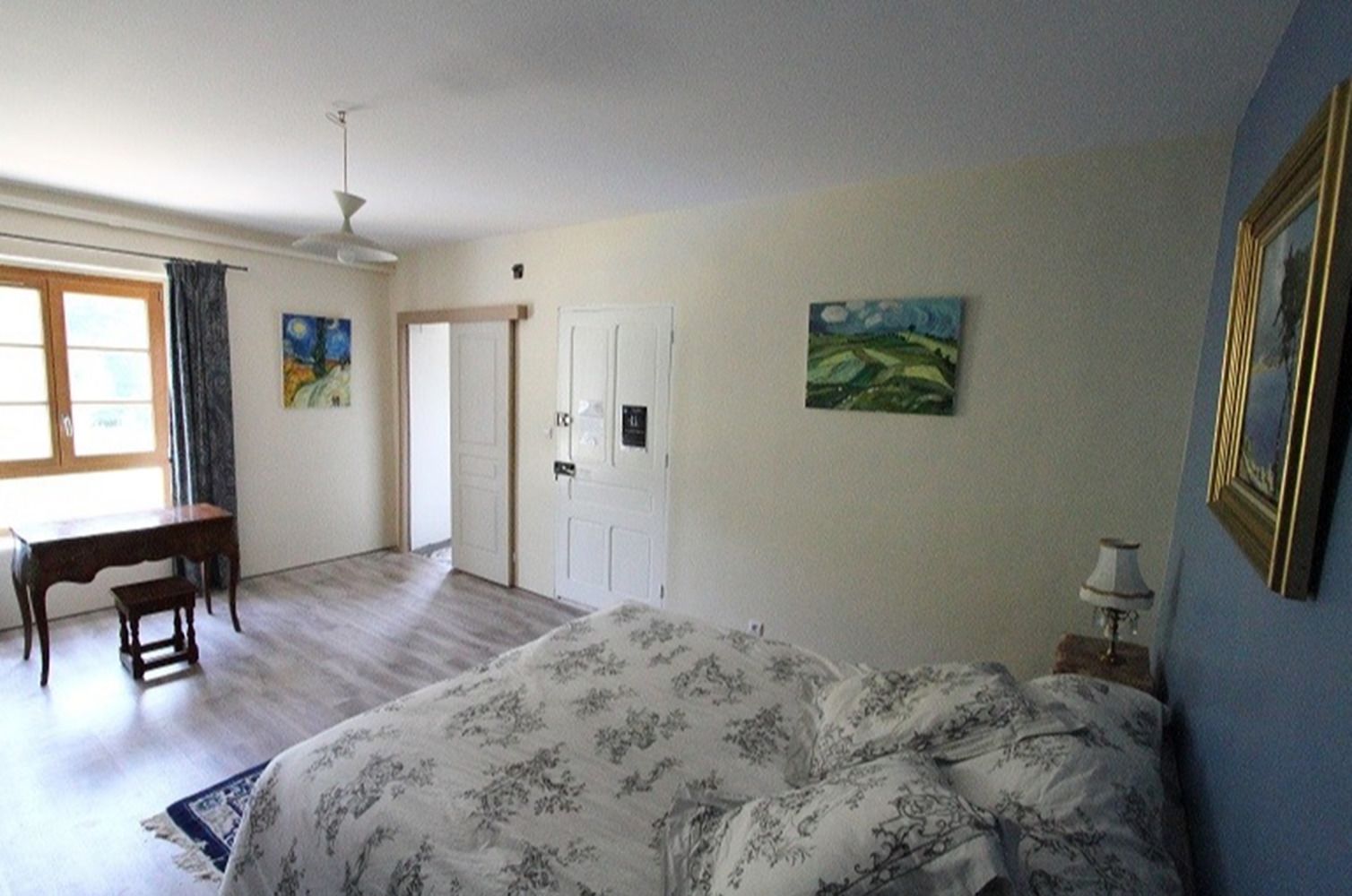 Um quarto com uma cama, uma escrivaninha, uma cadeira e duas portas.