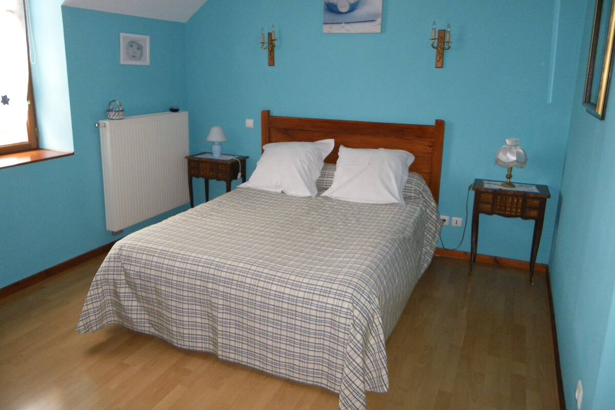 Quarto com cama, mesa de cabeceira, luminária, quadro na parede e janela.