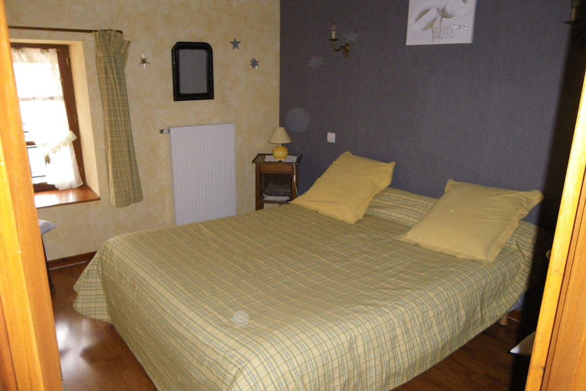 Quarto com uma cama grande, mesa de cabeceira, luminária, janela com cortinas e parede com detalhes de estrelas.