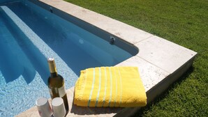 Uma piscina com uma toalha amarela e dois copos de vinho na borda.