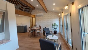 Um quarto espaçoso com teto de madeira, uma área de refeições com cadeiras e mesa, um sofá e um vaso com planta.