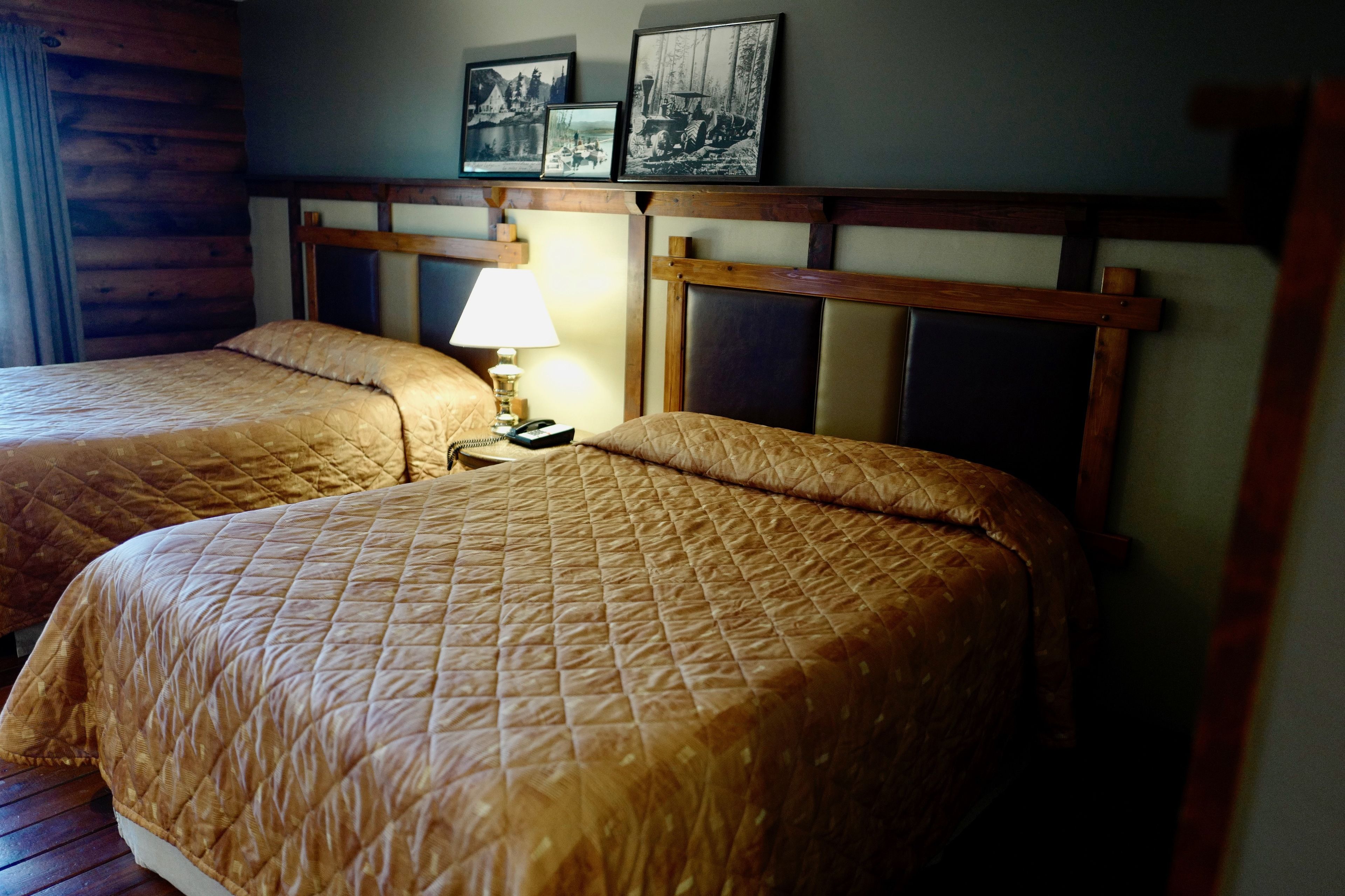 Quarto com duas camas, cabeceiras de madeira, mesa de cabeceira com abajur e quadros nas paredes.