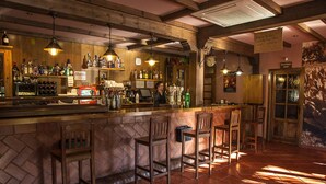 Uma área de bar com balcões de madeira, vários bancos e uma variedade de garrafas e copos nas prateleiras.