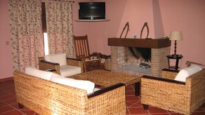Sala de estar com móveis de vime, lareira, televisão e cortina estampada.