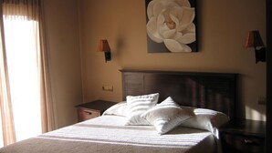 Uma cama bem arrumada com roupa de cama branca, uma grande obra de arte floral na parede e duas luminárias de cabeceira.