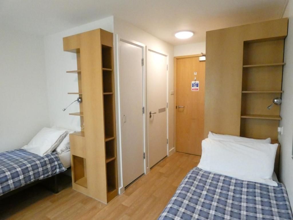 Quarto com duas camas, estantes de madeira e uma porta.