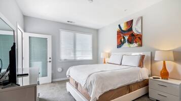 Quarto com cama, mesas de cabeceira, escrivaninha e janela com persianas.