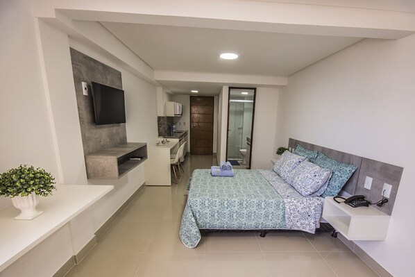 Quarto moderno com cama, mesa de cabeceira e televisão na parede.