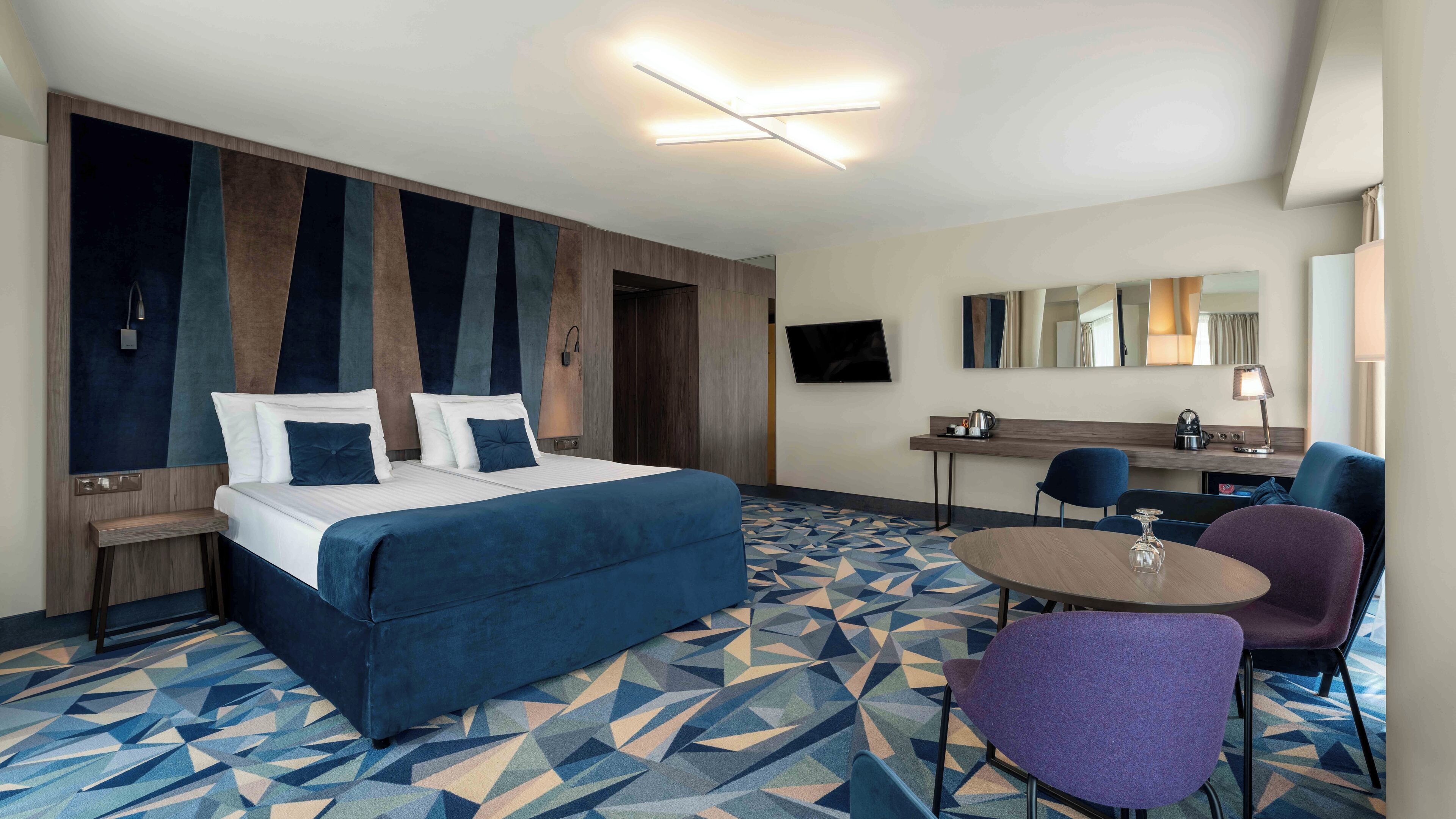 Quarto de hotel com uma cama grande, uma escrivaninha, uma cadeira e uma pequena mesa.
