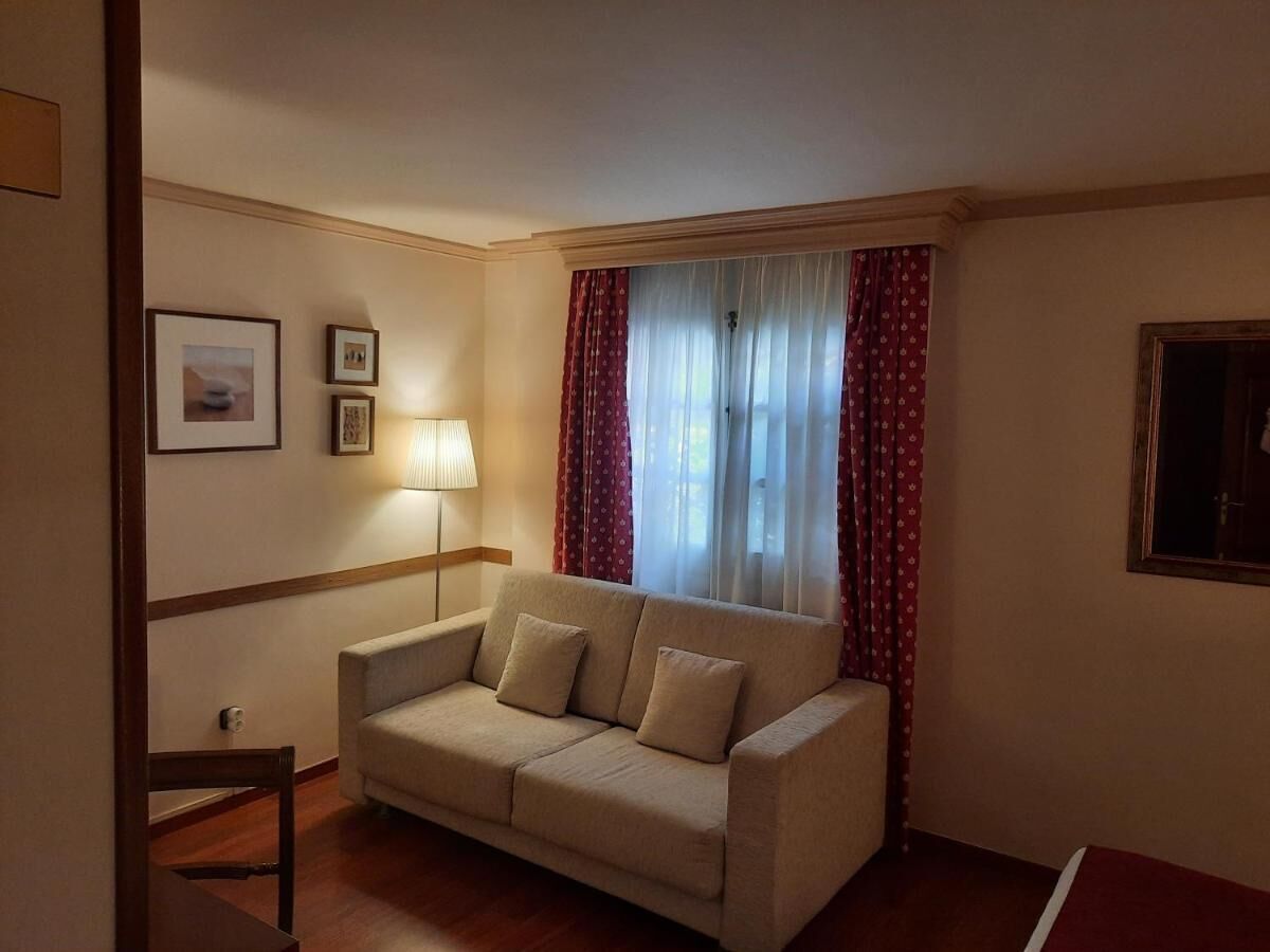 Um quarto com um sofá bege, um abajur e uma janela com cortinas vermelhas.