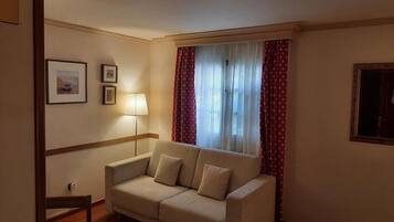 Um quarto com um sofá bege, um abajur e uma janela com cortinas vermelhas.