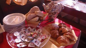Buffet de café da manhã com pães, croissants e potes de iogurte.