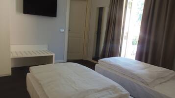 Quarto de hotel com duas camas, uma televisão de tela plana fixada na parede, uma mesinha de cabeceira e uma porta que dá para outro cômodo.