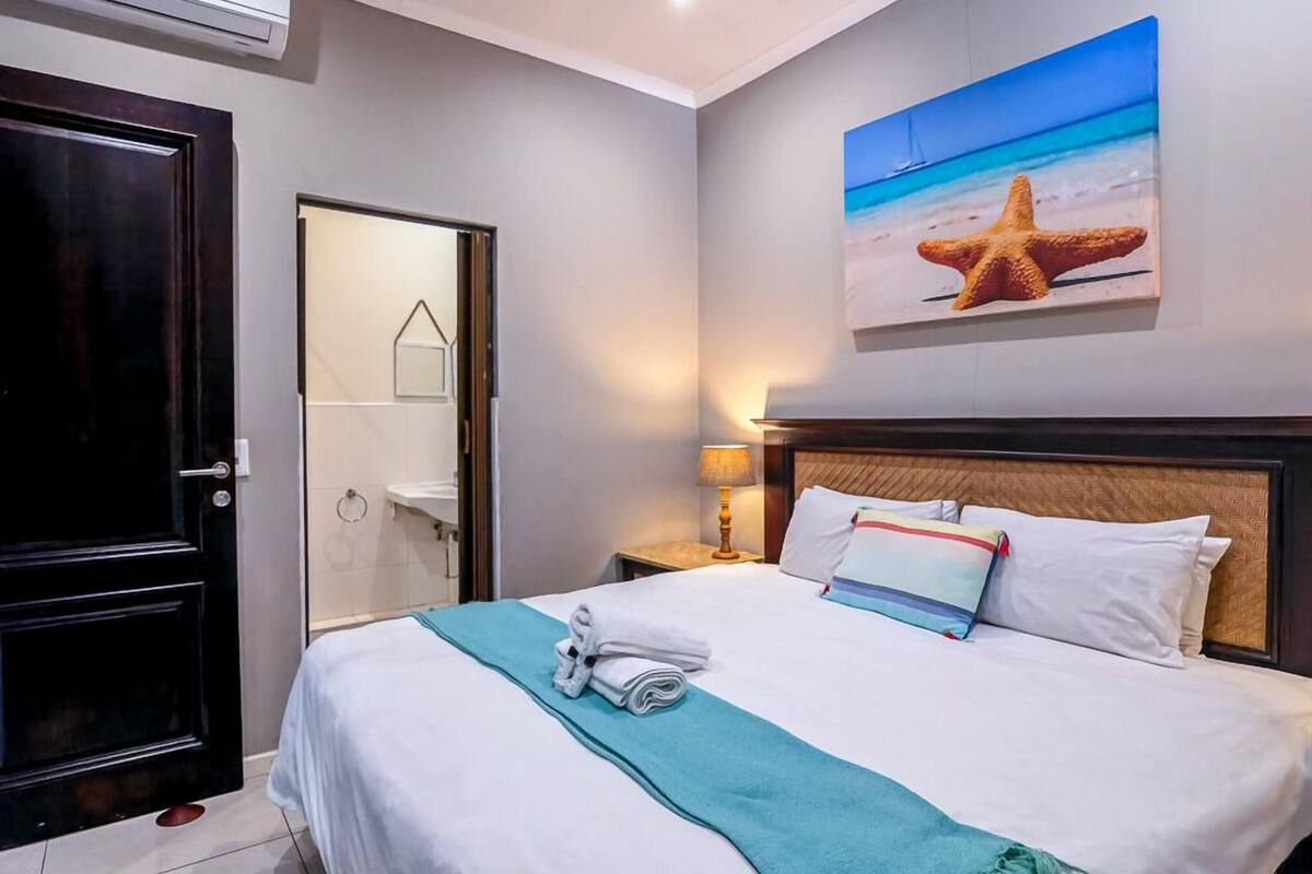 Quarto de hotel com uma cama, uma pintura de estrela-do-mar na parede, um banheiro visível através de uma porta aberta e uma toalha na cama.