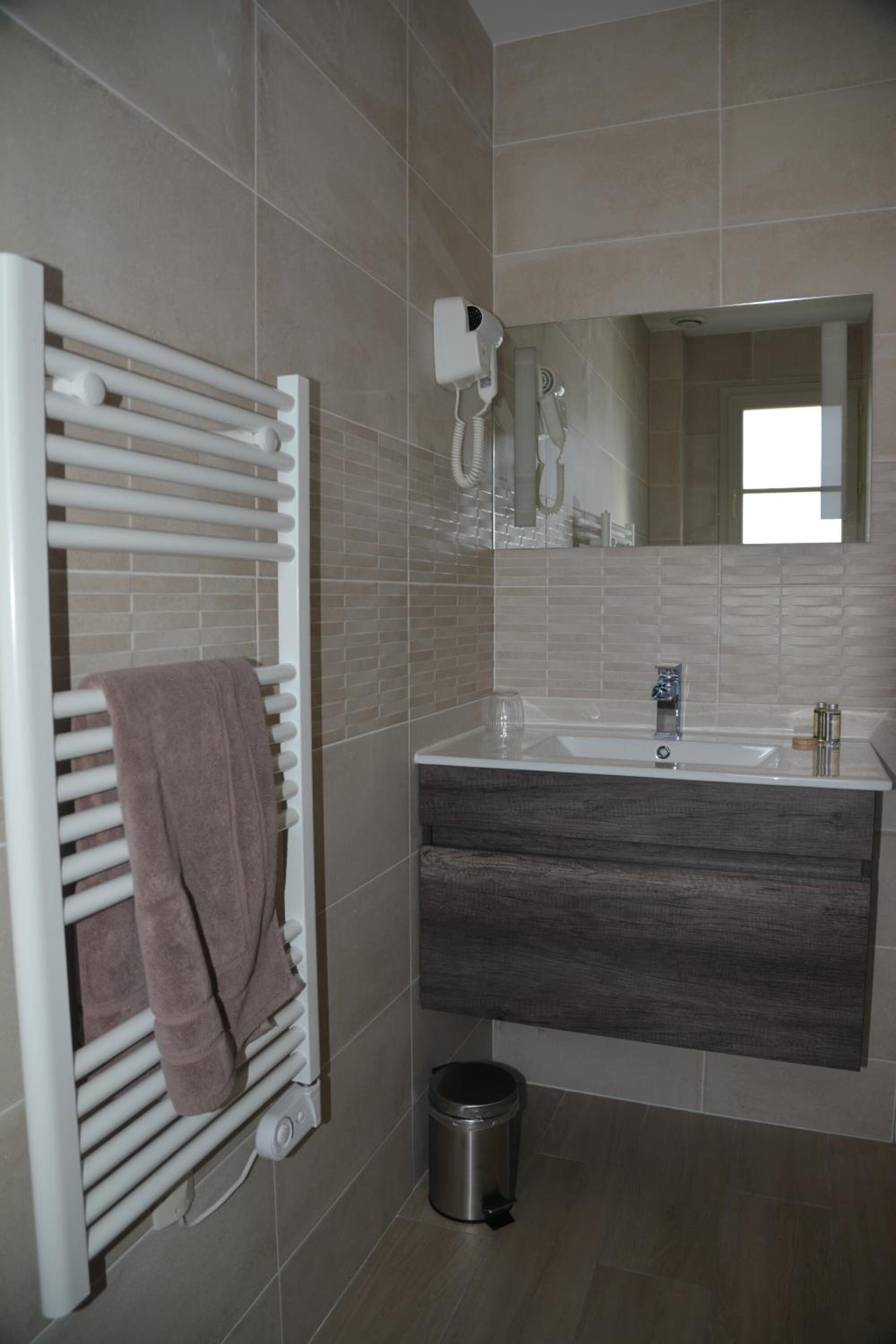 Uma casa de banho moderna com um porta-toalhas branco, uma pia com espelho em cima e um cestinho de lixo.