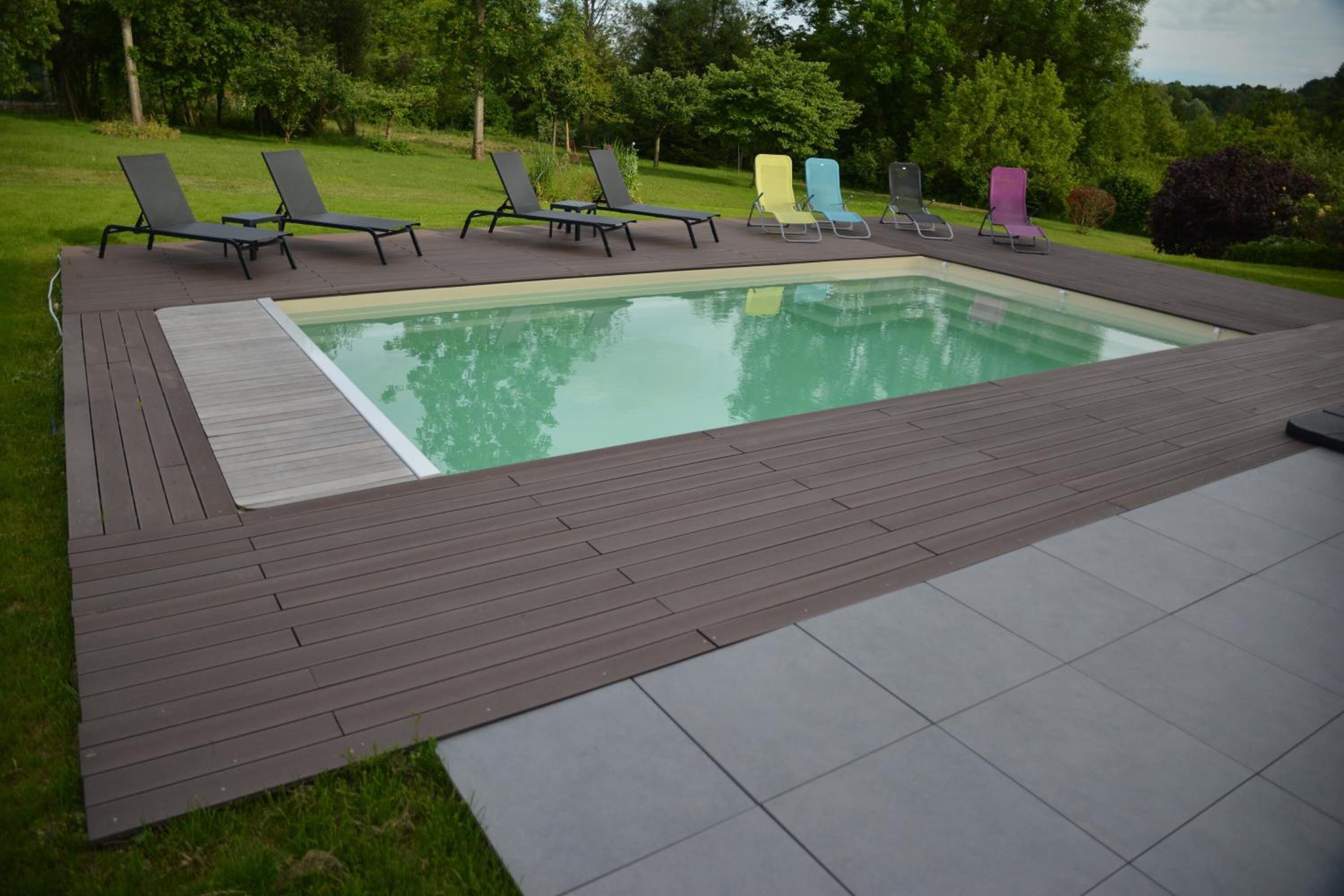 Piscina retangular com deck de madeira e área revestida com azulejos.