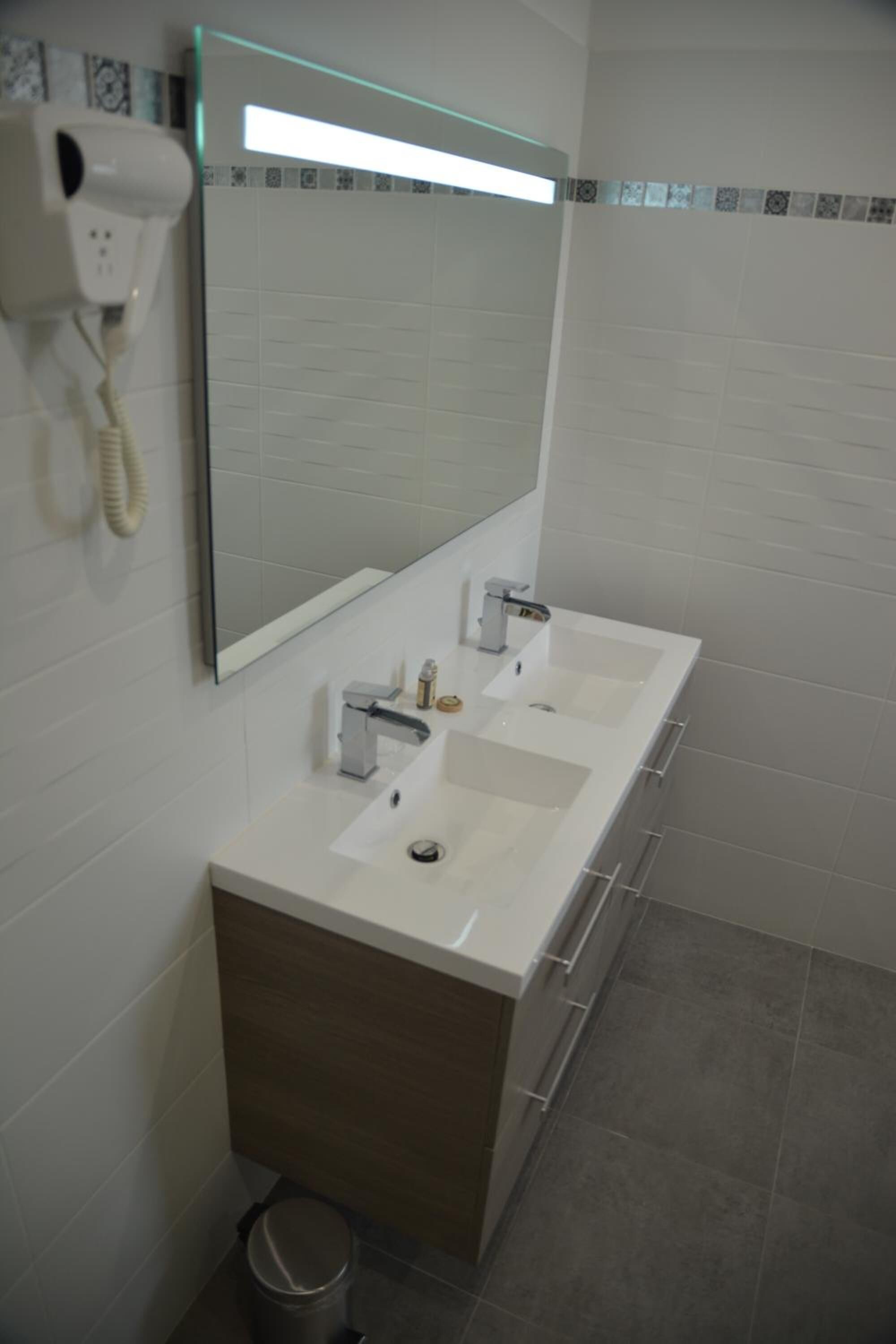 Casa de banho com duas pias, um espelho, um secador de cabelo e um cesto de lixo.
