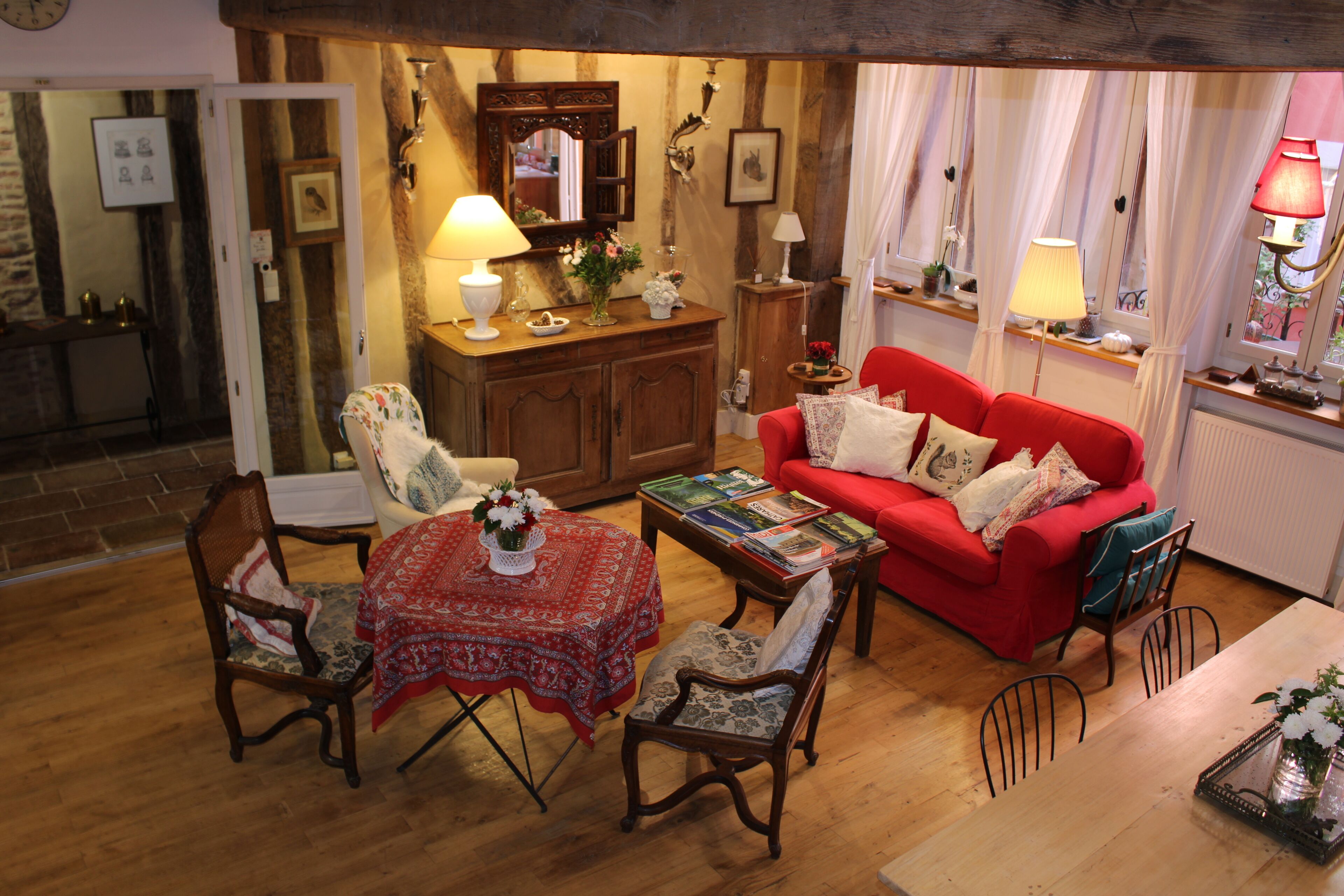 Uma sala de estar acolhedora com um sofá vermelho, cadeiras de madeira, uma mesa de centro e uma lareira.