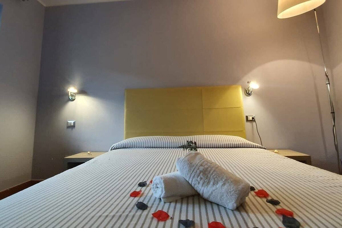 Quarto de hotel com uma cama, cabeceira, abajures e uma luminária de chão.
