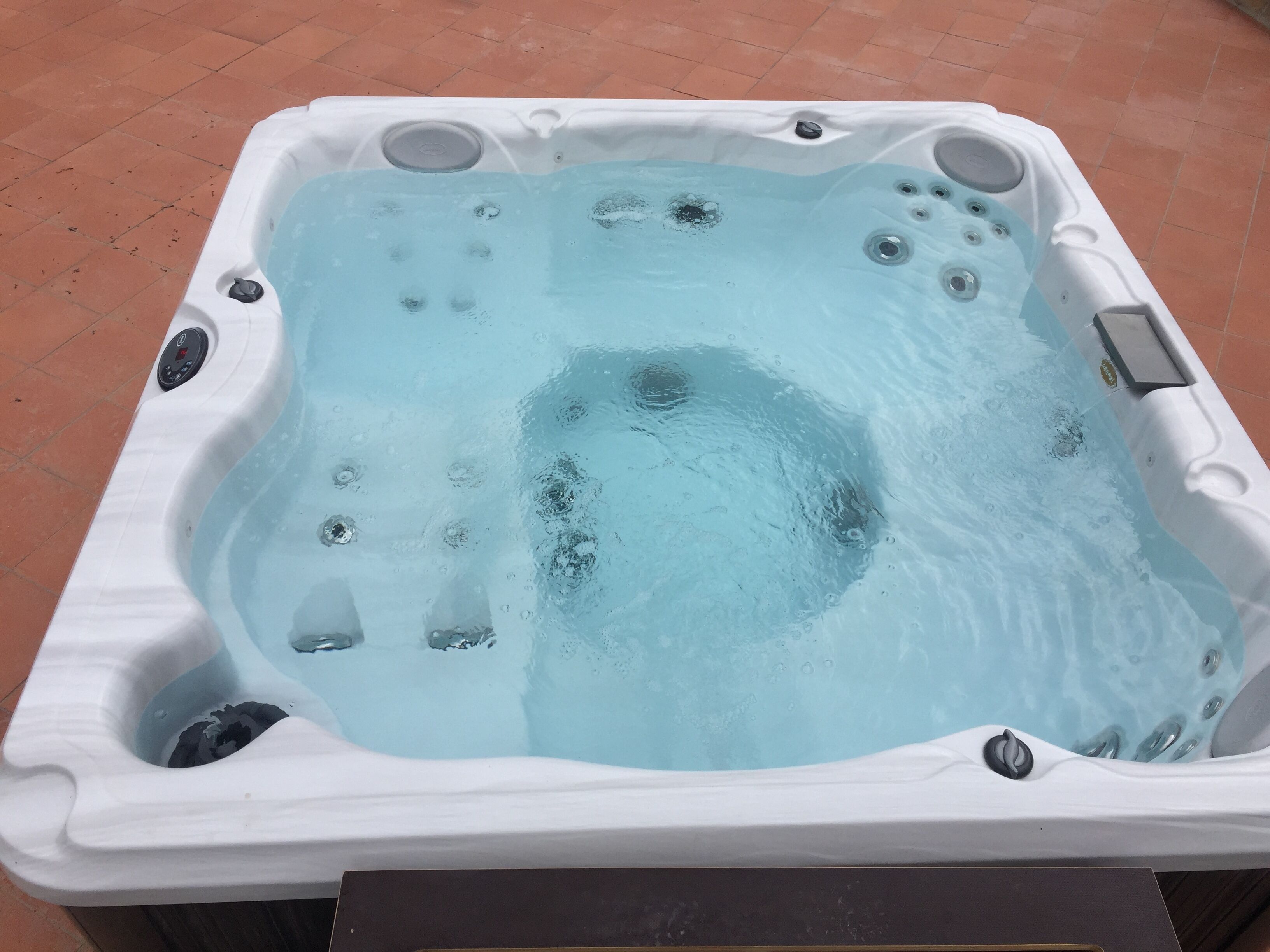 Uma banheira de hidromassagem com painel de controle, borbulhas e piso ladrilhado.