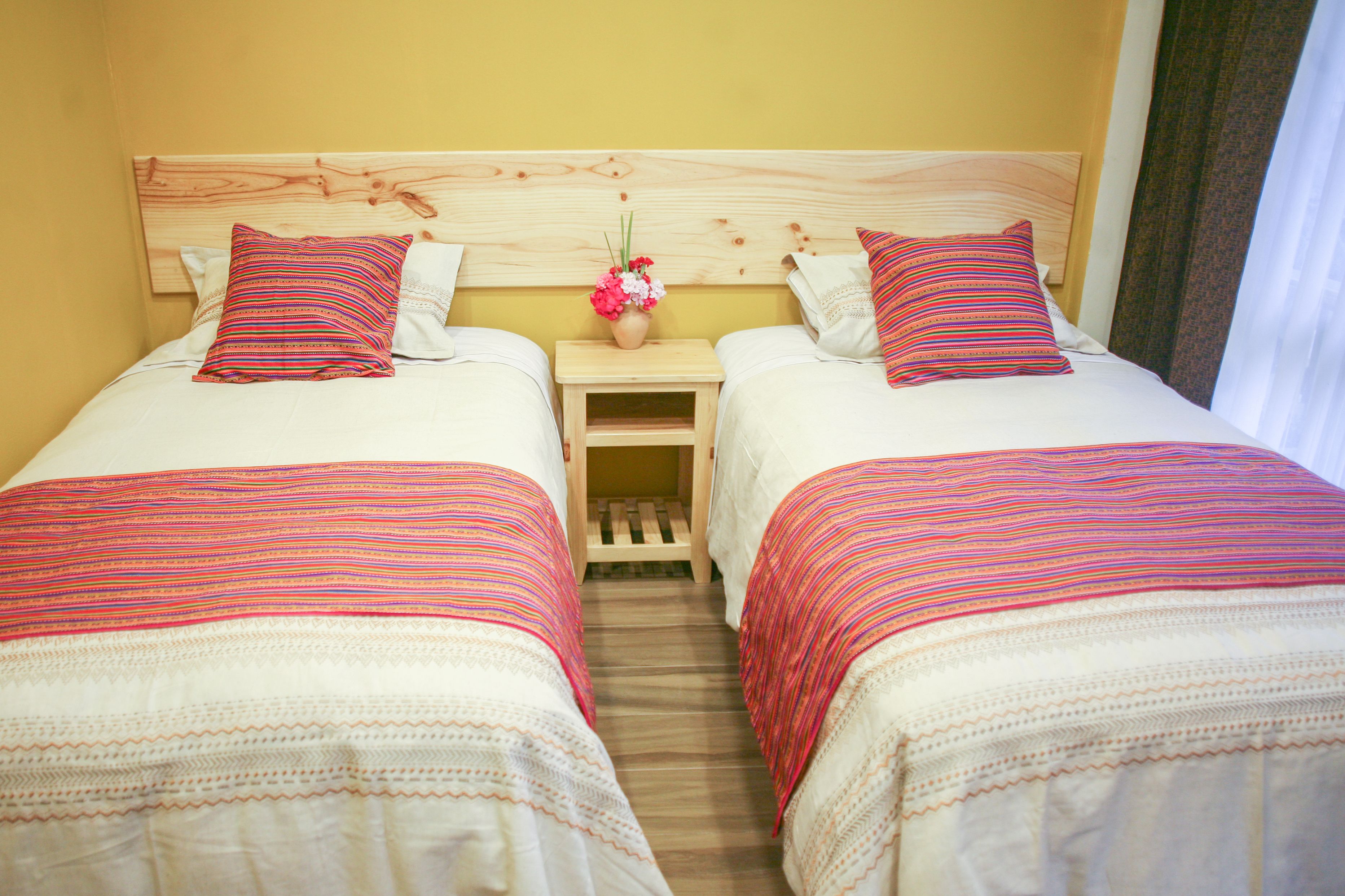 Quarto duplo com duas camas, cada uma com cabeceira de madeira, roupa de cama branca e almofadas listradas.