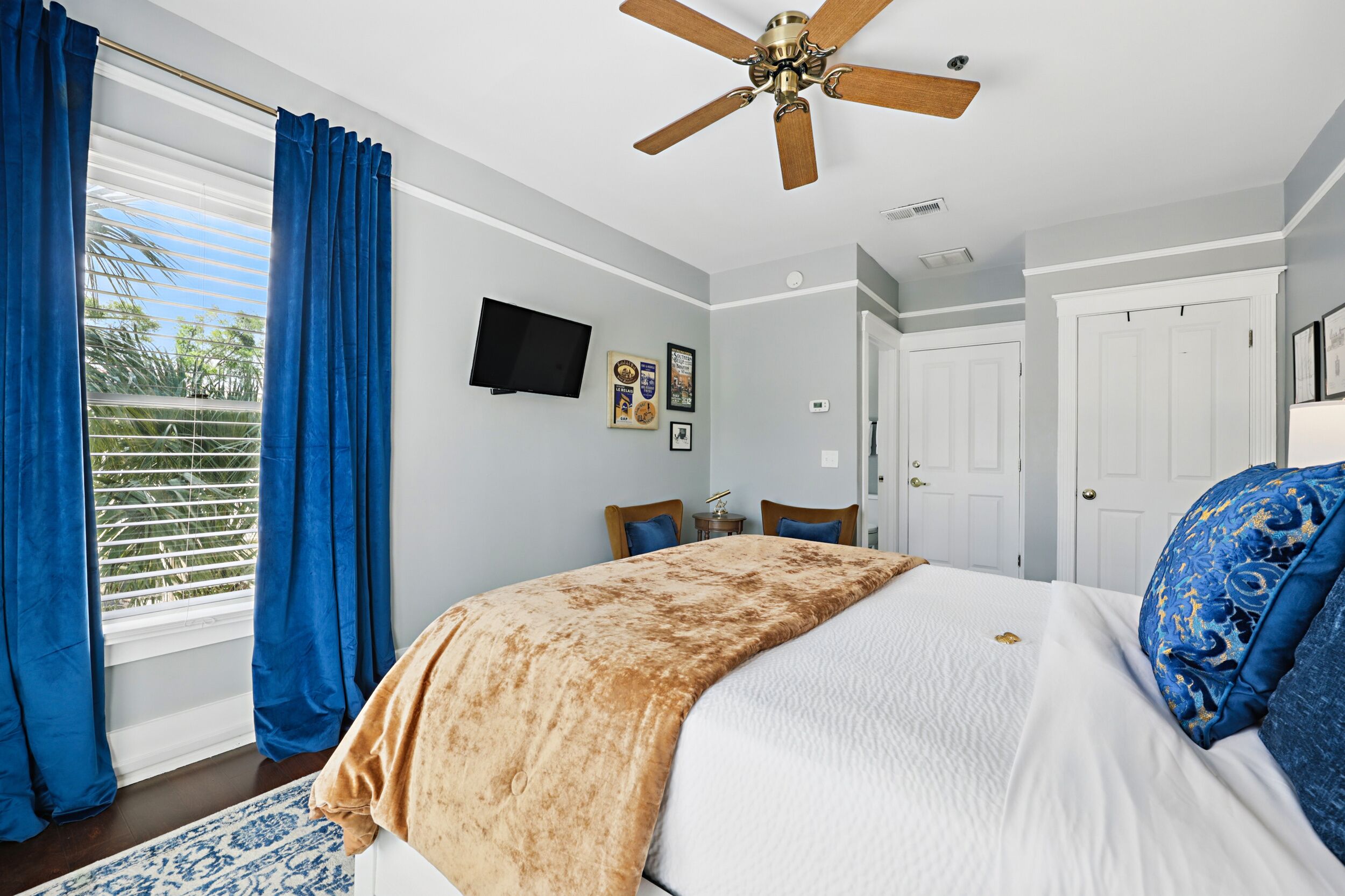 Quarto com cama, ventilador de teto, televisão e janela com cortinas.