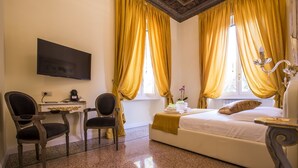 Quarto de hotel com cama, duas cadeiras, escrivaninha, TV de tela plana e janela com cortinas amarelas.