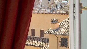 Vista da janela com cortina, mostrando um horizonte urbano com edifícios tradicionais e uma torre.