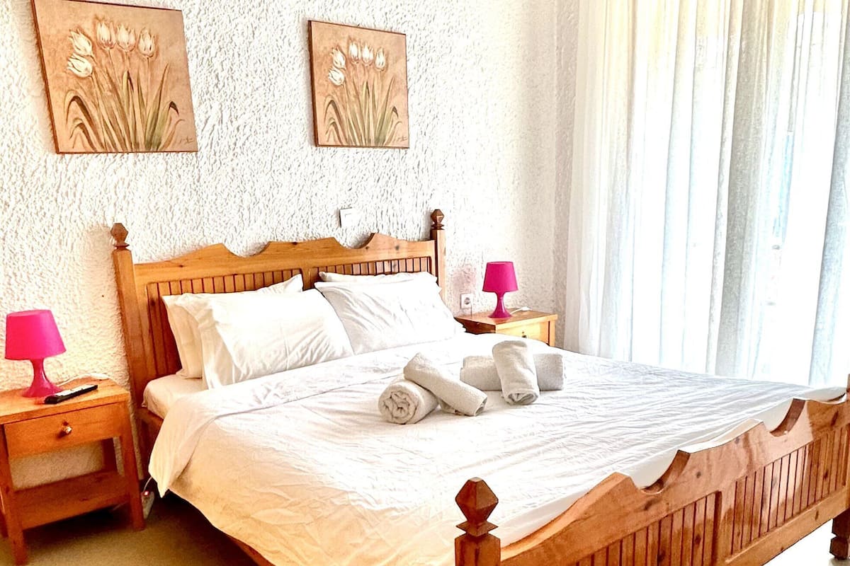 Uma cama de madeira com roupa de cama branca, duas mesas de cabeceira com abajures e uma obra de arte na parede.
