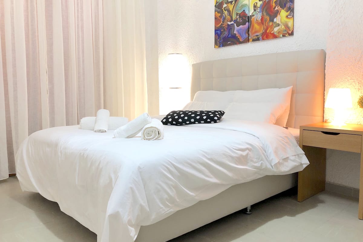 Cama bem arrumada com lençóis brancos, almofada com bolinhas pretas e toalhas dobradas.