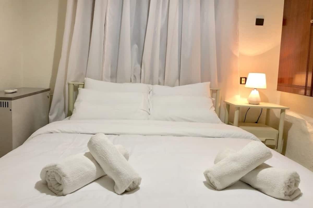 Cama bem arrumada com lençóis brancos e duas toalhas sobre ela.