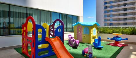 Uma área de lazer ao ar livre com escorrega, estruturas de escalada e uma casinha.